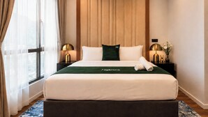 Quarto de hotel com uma cama, mesa de cabeceira, abajur, janela com cortinas e vista exterior.