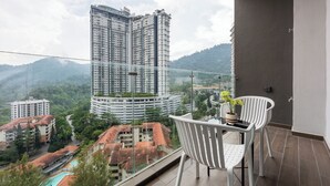 Uma varanda com cadeira e mesa brancas, com vista para um horizonte urbano com edifícios altos e montanhas ao fundo.