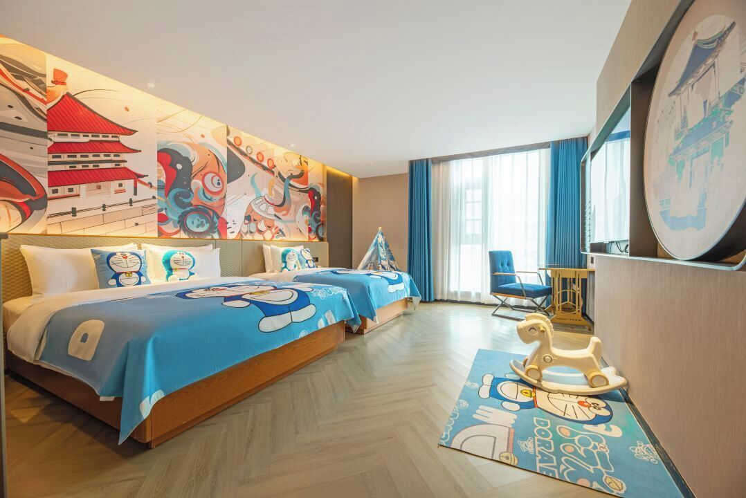 Quarto de hotel com duas camas, um mural grande na parede, um cavalinho de balanço e vista para a cidade.