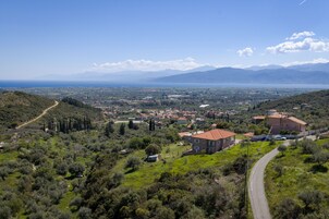 Paisagem acidentada com uma estrada serpenteando por uma área residencial, casas com telhados vermelhos e montanhas ao longe.