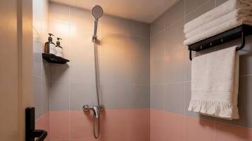 Casa de banho com chuveiro, porta-toalhas com toalhas dobradas e uma prateleira com artigos de higiene pessoal.