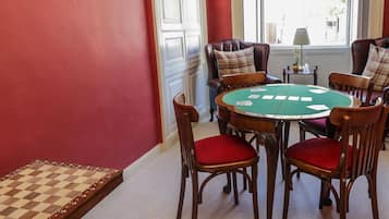 Quarto com uma mesa redonda, cadeiras, um tabuleiro de xadrez e uma janela com vista.