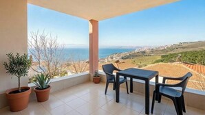 Varanda com mesa, cadeiras, plantas em vasos e vista para o mar e a cidade.