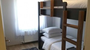 Quarto com beliche, janela, radiador e tapete escuro.