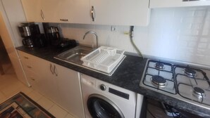 Uma cozinha compacta com máquina de lavar, pia, fogão e cafeteira.