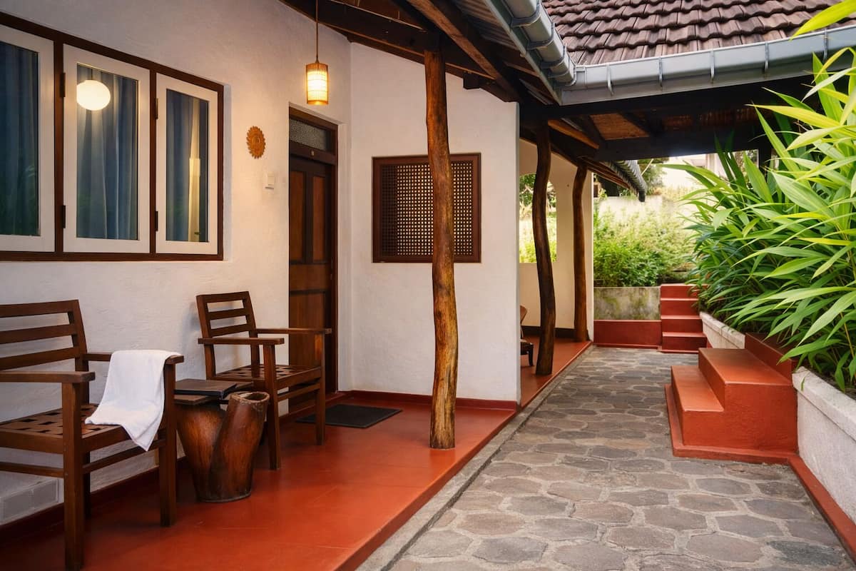 Uma área de estar coberta ao ar livre, com cadeiras e mesa de madeira, um caminho de pedra e um poste de madeira.