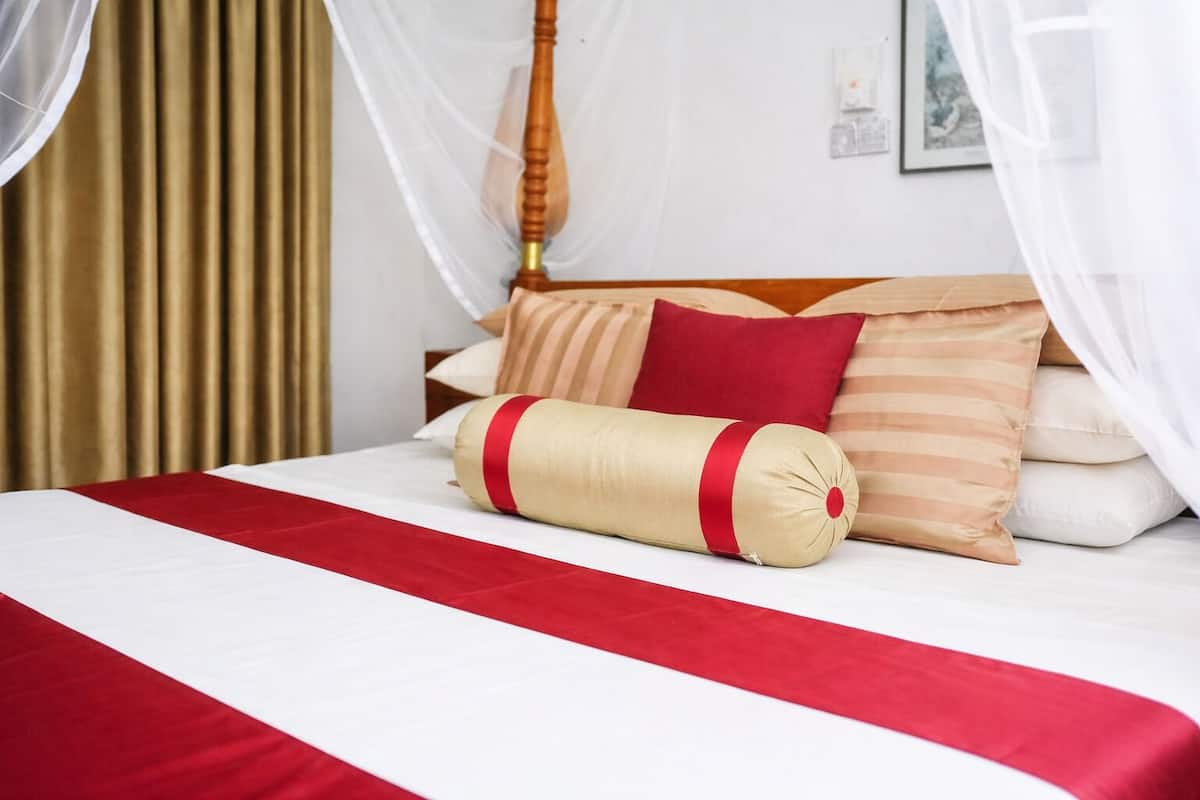 Uma cama com colcha listrada em vermelho e branco, um travesseiro bege com faixa vermelha e uma cabeceira de madeira.