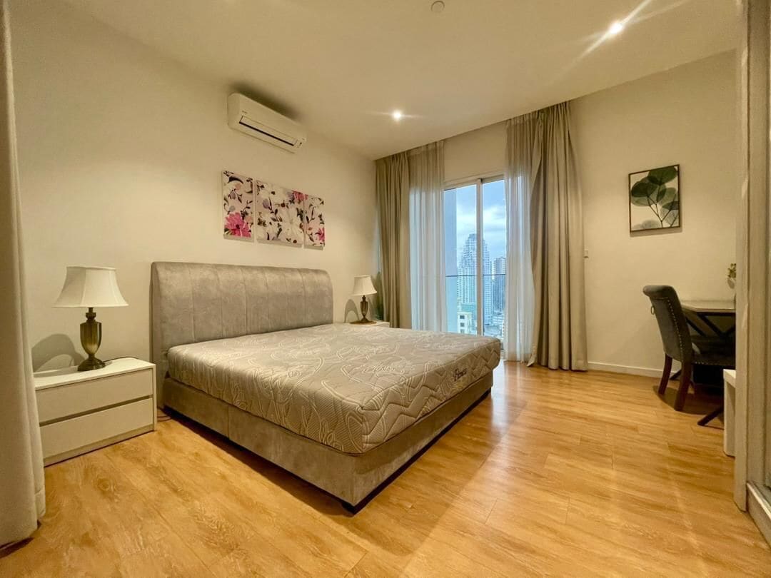 Quarto de hotel com uma cama grande, mesas de cabeceira com abajures, uma escrivaninha e vista para a cidade.
