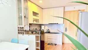 Uma cozinha moderna com armários de madeira, uma área de refeições com mesa e cadeiras brancas, e uma geladeira.