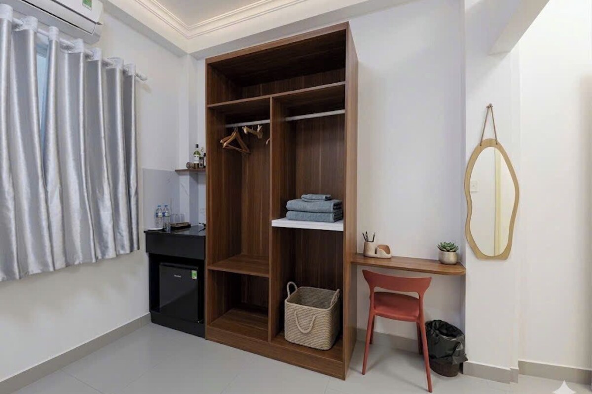 Quarto com guarda-roupa, escrivaninha, cadeira, espelho e pequena estante.