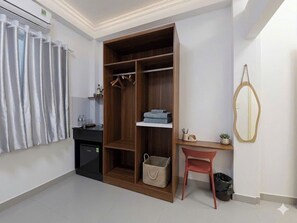 Quarto com guarda-roupa, escrivaninha, cadeira, espelho e pequena estante.