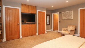 Um quarto com cama, televisão, armários de madeira e uma cadeira.