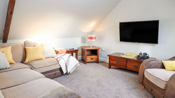 Quarto estilo loft com teto alto, televisão de tela plana na parede, mesa de centro de madeira, sofá e uma pequena mesa lateral.