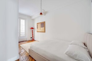 Um quarto com uma cama, uma janela, um abajur vermelho e um quadro na parede.