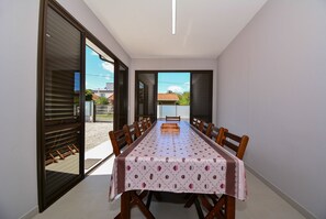 Uma sala de jantar com mesa posta para seis pessoas, uma porta de vidro deslizante e vista para o exterior.