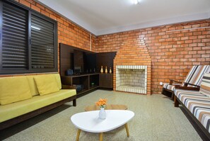 Uma sala de estar com sofá, mesa de centro, televisão, lareira e parede de tijolos.