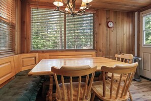 Uma sala de jantar com piso de madeira, um banco, uma mesa e um lustre.