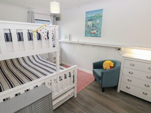Uma cama beliche com roupa de cama listrada, uma cadeira com almofada, um penteado com gavetas, um quadro na parede e um tapete vermelho.