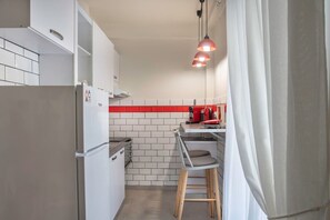 Uma cozinha compacta com armários brancos, um painel de parede vermelho e uma única luminária pendente vermelha.