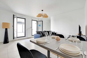 Uma sala de jantar moderna com uma mesa posta para quatro pessoas, um sofá, uma luminária e vista através de uma porta de vidro.