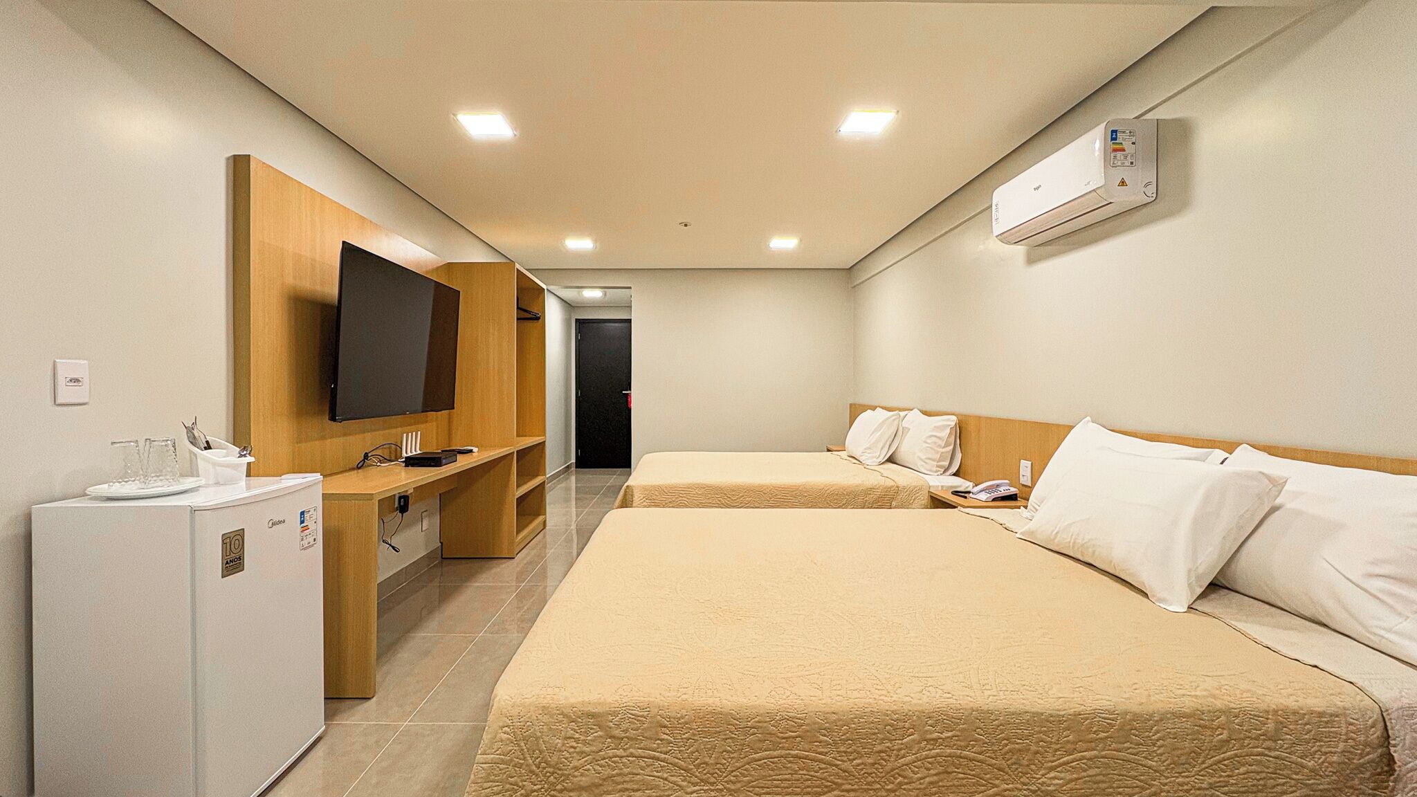 Quarto de hotel com duas camas, televisão, escrivaninha e frigorífico.