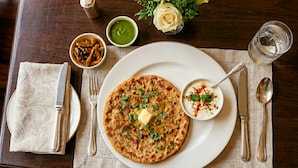 Uma mesa de jantar com um prato de comida, um recipiente com molho, um copo de água e um vaso com uma flor.