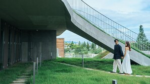 Uma estrutura arquitetônica moderna com uma cobertura de concreto e guarda-corpo de metal, uma área gramada e céu limpo.