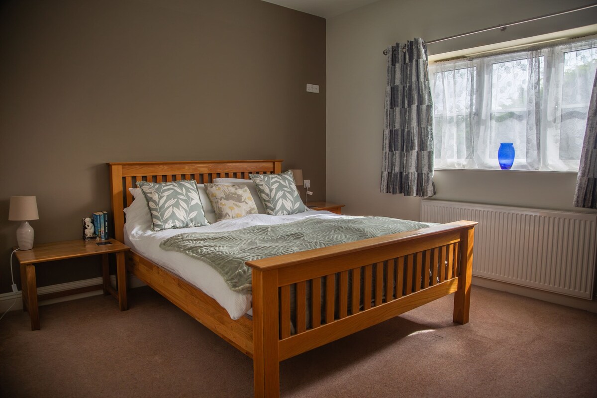 Quarto com cama de madeira, mesa de cabeceira, luminária, janela com cortinas e radiador.