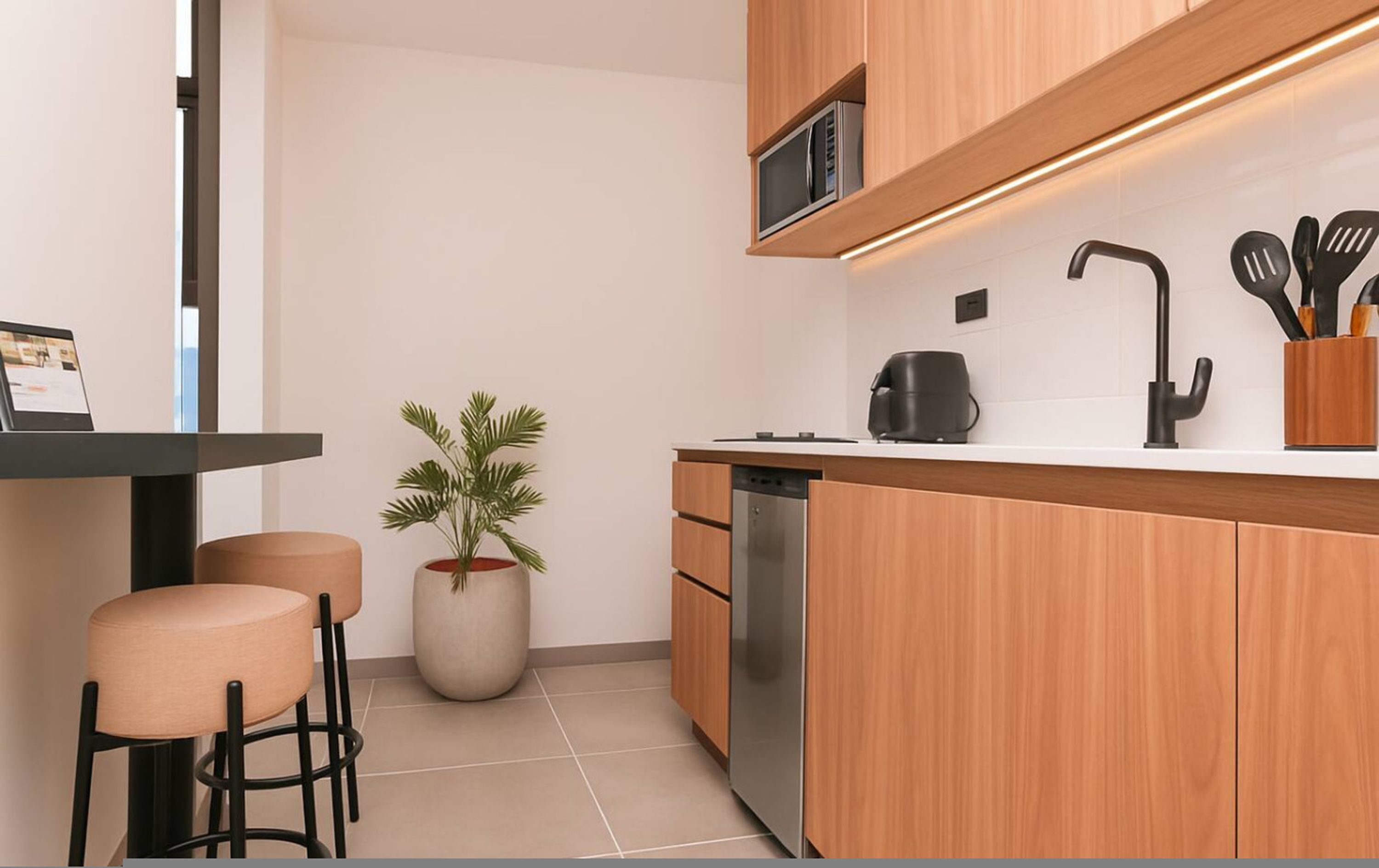 Uma cozinha moderna com armários de madeira, micro-ondas embutido, máquina de café e lava-louças. Há dois bancos e um vaso de planta.