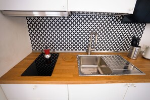 Cozinha com pia de aço inoxidável, tapete preto e chaleira vermelha.