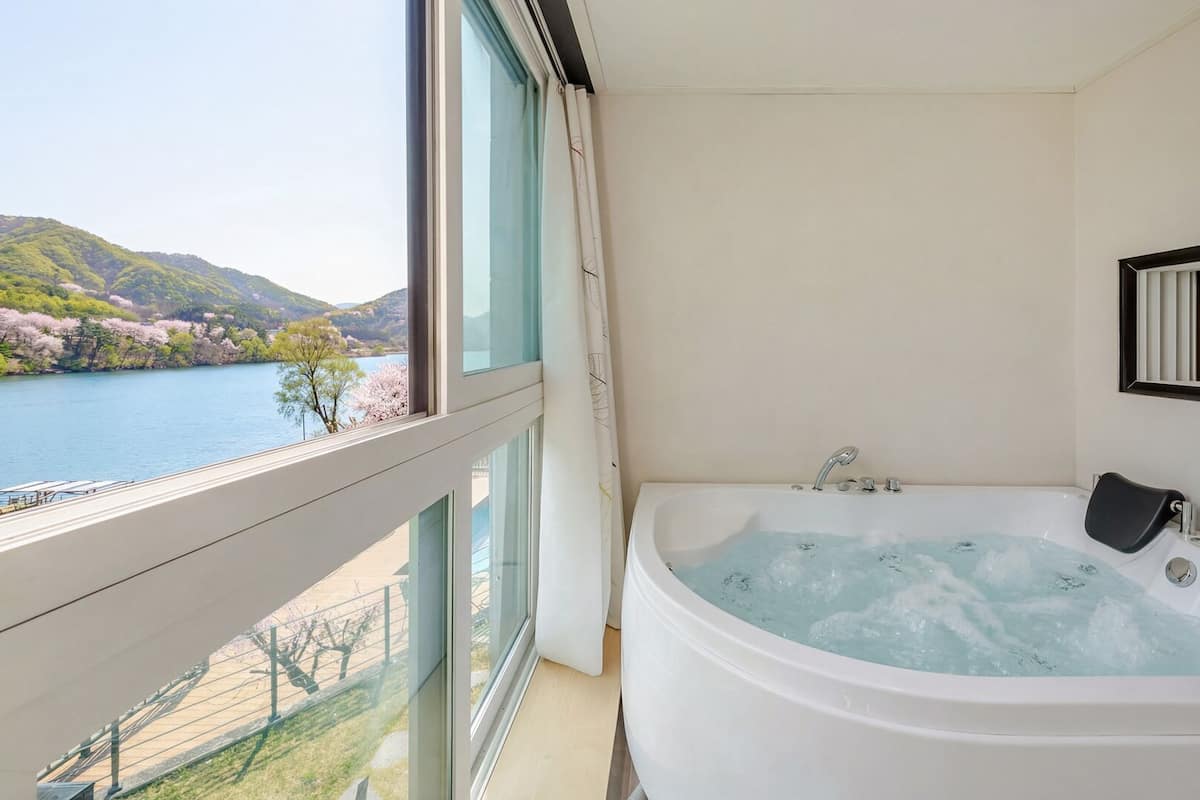Um banheiro com banheira, uma janela com vista para um lago e colinas, e um espelho.