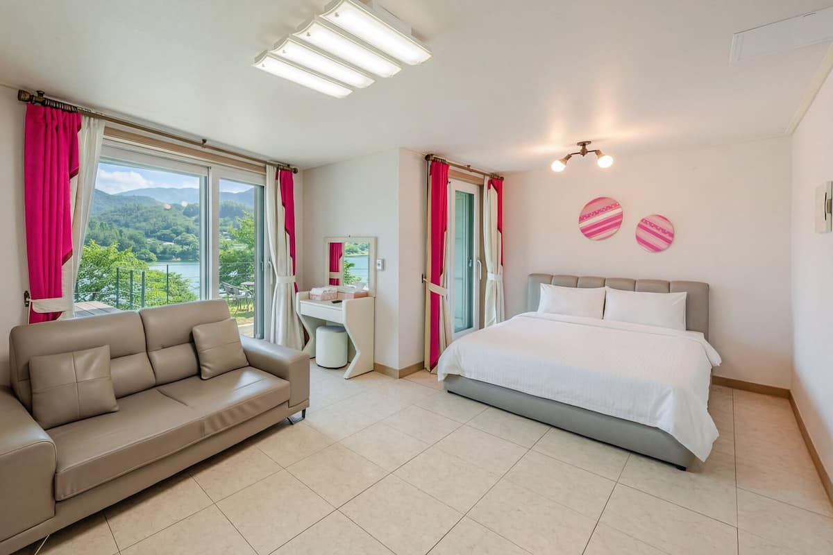 Quarto com cama, penteadeira, sofá e vista para o exterior.