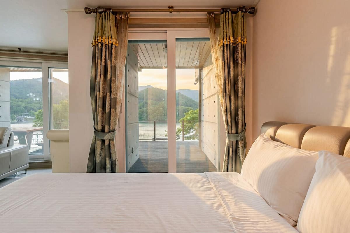 Quarto com cama, vista para um lago e varanda com cortinas.