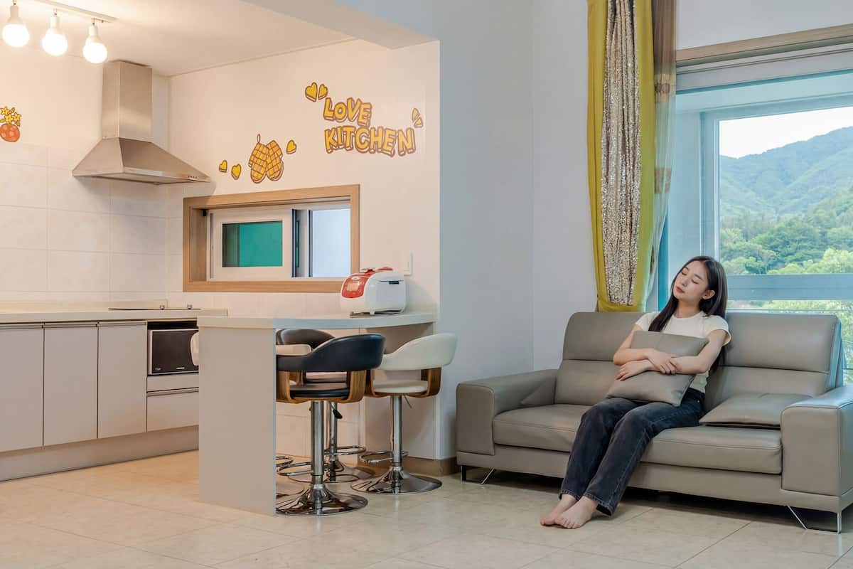 Uma sala de estar moderna com sofá, espaço de cozinha e uma janela grande com vista para o verde.