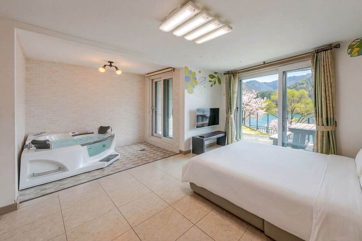 Quarto de hotel com cama, televisão, banheira e varanda com vista para montanhas e cerejeiras.