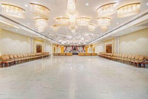 Uma sala de conferências ampla com uma longa mesa e fileiras de cadeiras, grandes lustres e piso lustroso.