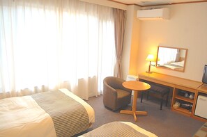 Quarto de hotel com uma cama, escrivaninha, cadeira, abajur, espelho e televisão.
