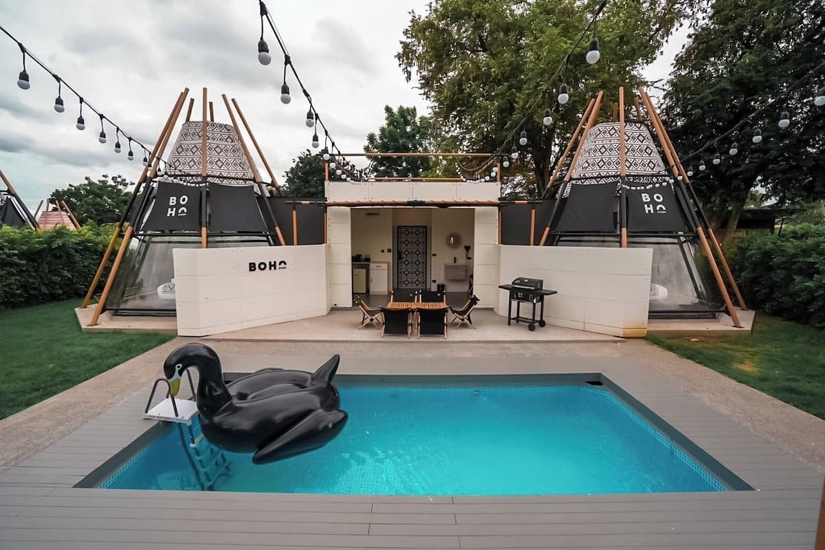 Uma piscina com duas tendas com a etiqueta 'BOHO' e uma decoração com cisne negro.