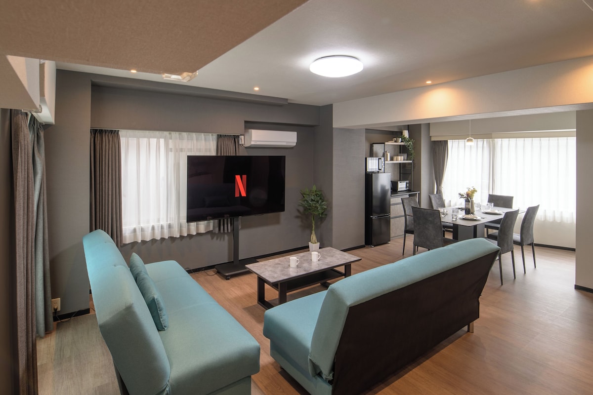 Uma sala de estar moderna com sofá, mesa de centro, televisão de tela plana e área de jantar com cadeiras e mesa.