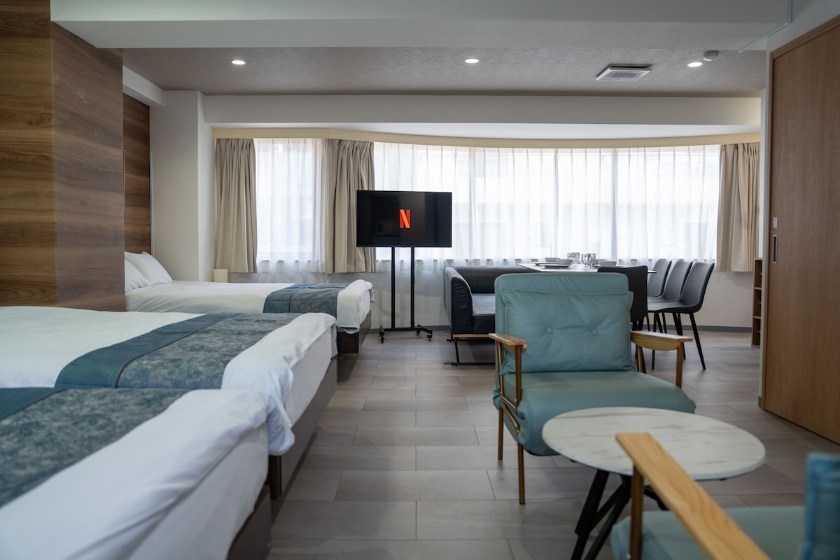 Quarto de hotel com duas camas, televisão, mesa de jantar e área de estar.