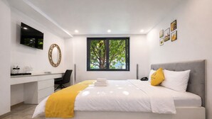 Quarto de hotel moderno com cama, escrivaninha e janela com vista para árvores.