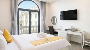 Quarto de hotel com cama, escrivaninha, cadeira, televisão e varanda com vista para edifícios.