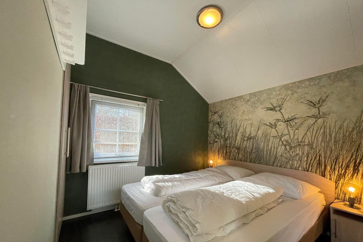 Quarto com cama, janela com cortinas, radiador e parede com painel de bambu.