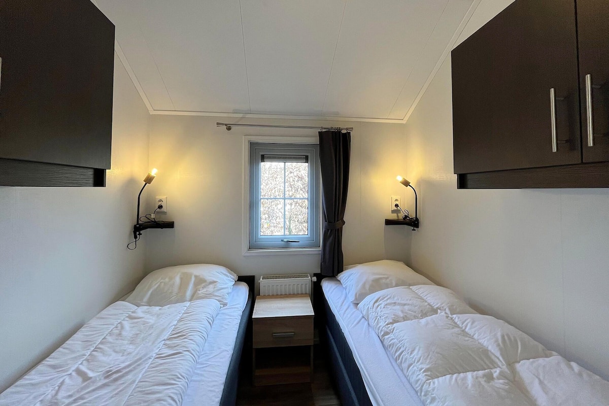 Quarto pequeno e bem iluminado, com duas camas de solteiro, janela com cortinas e luminárias na parede.