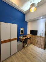 Quarto de hotel com escrivaninha, guarda-roupa e televisão.