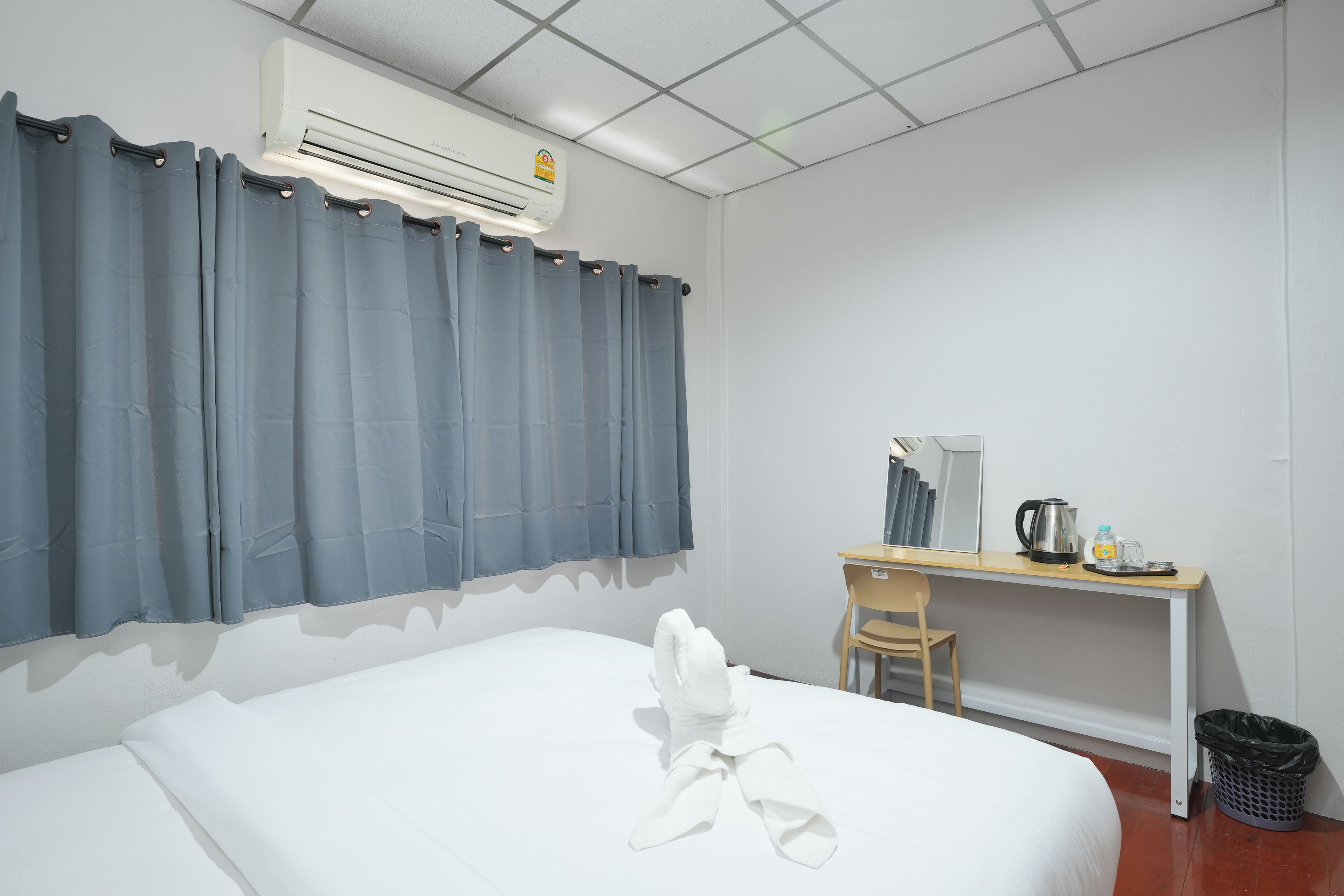 Quarto de hotel com cama, escrivaninha com cadeira, ar condicionado e lixeira.