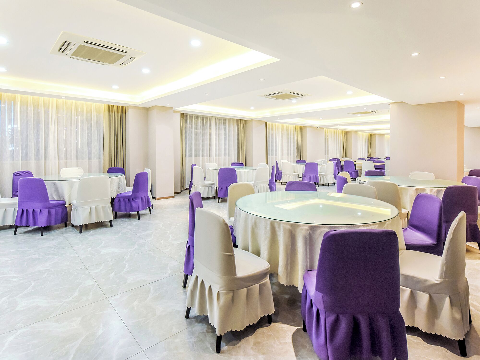 Uma sala de conferências de hotel com mesas redondas, cadeiras roxas e toalhas de mesa brancas.