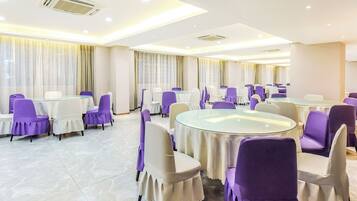 Uma sala de conferências de hotel com mesas redondas, cadeiras roxas e toalhas de mesa brancas.