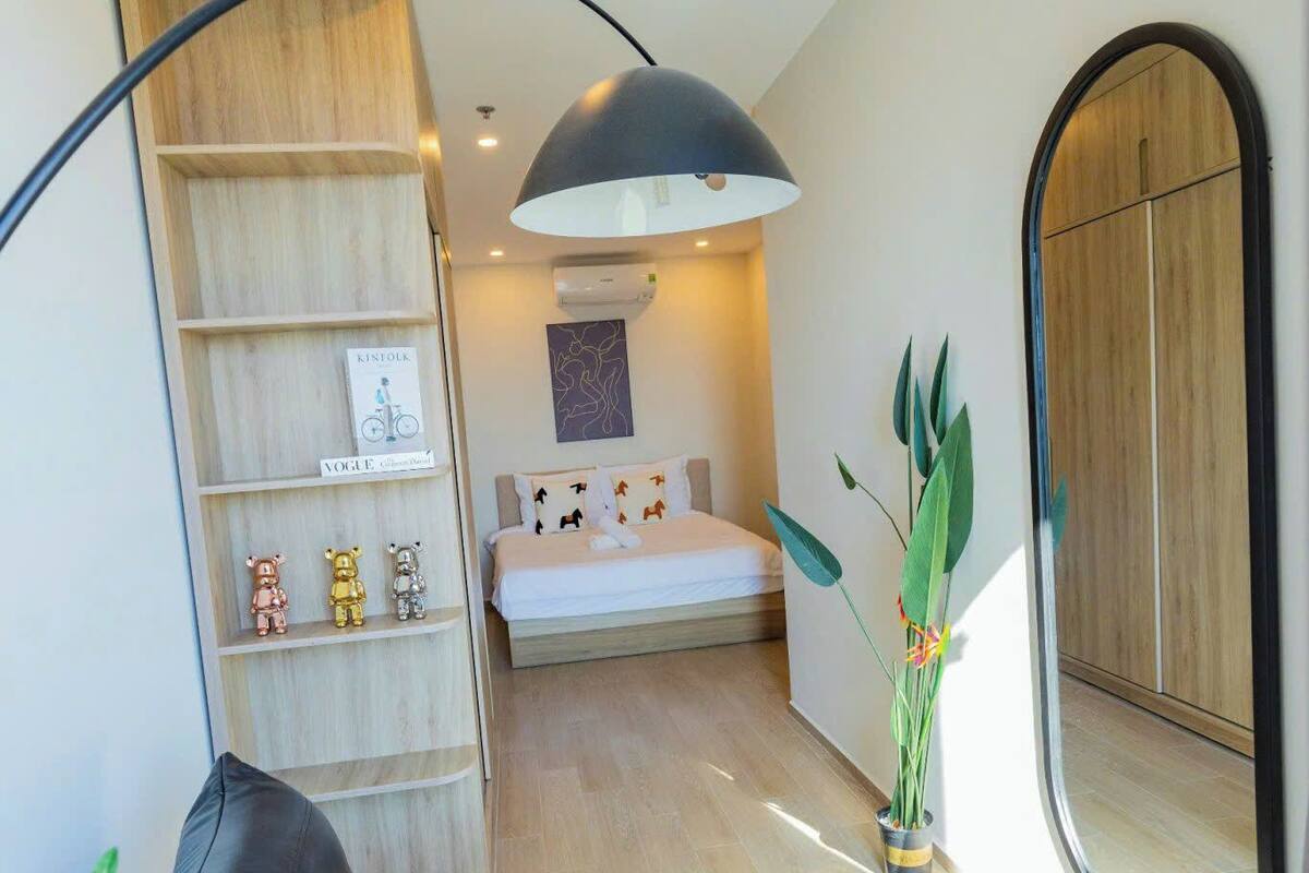 Um quarto moderno com uma cama, um sofá de couro preto, uma estante de madeira e um espelho.