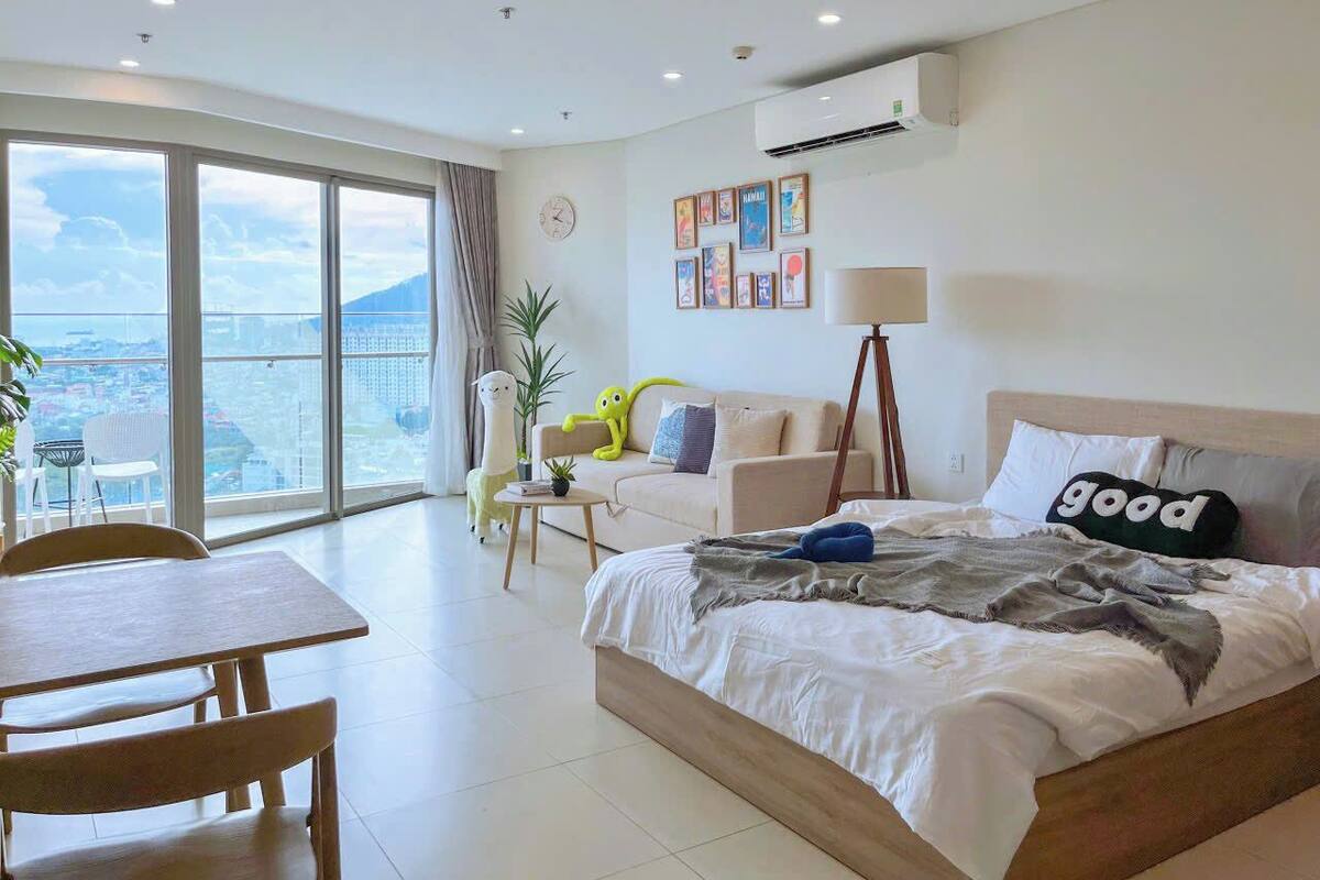 Quarto de hotel com uma cama grande, uma mesa de jantar, um sofá, uma varanda com vista e uma parede com quadros.